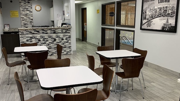 Uma sala de jantar moderna com mesas brancas e cadeiras castanhas, uma mesa de recepção com um relógio e um quadro de Lincoln na parede.