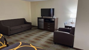 Quarto de hotel com sofá, uma cadeira, televisão sobre um móvel e uma luminária.
