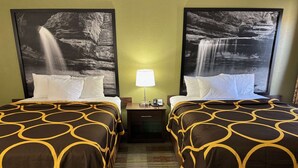 Quarto de hotel com duas camas, cada uma com colcha estampada, mesa de cabeceira e luminária, e quadro com pintura de uma cascata na parede.