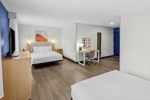 Quarto de hotel com cama, escrivaninha e um quadro na parede.