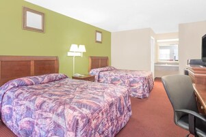 Quarto de hotel com duas camas, uma mesa, uma cadeira e uma televisão.