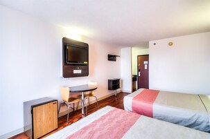 Quarto de hotel com duas camas, uma mesa, uma cadeira, uma televisão e um pequeno armário.