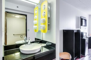 Uma casa de banho moderna com uma bacia redonda, um espelho com suportes de toalha amarelos e uma sanita preta.