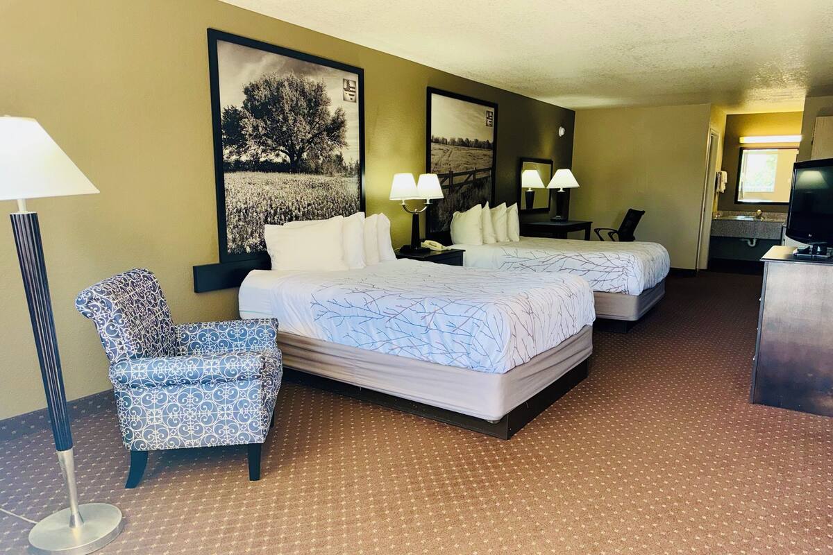 Quarto de hotel com duas camas, uma cadeira, uma escrivaninha e uma televisão.