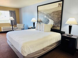 Quarto de hotel com uma cama grande, duas mesas de cabeceira com luminárias, uma cadeira e um quadro grande na parede.
