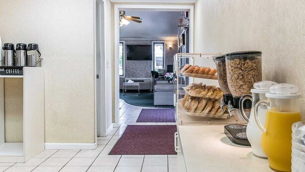 Uma área de cozinha de hotel com estação de café, dispensador de suco e balcão de café da manhã com pães e granola.