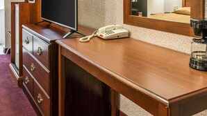 Uma mesa de madeira com uma televisão de tela plana, um telefone e uma cafeteira.