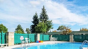 Uma piscina com cerca verde, algumas cadeiras e uma placa na cerca.
