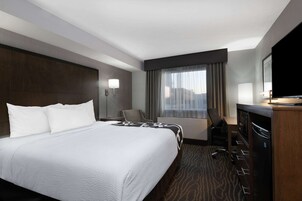 Quarto de hotel com uma cama grande, uma mesa com televisão de tela plana, uma cadeira, abajur e uma janela com cortinas.