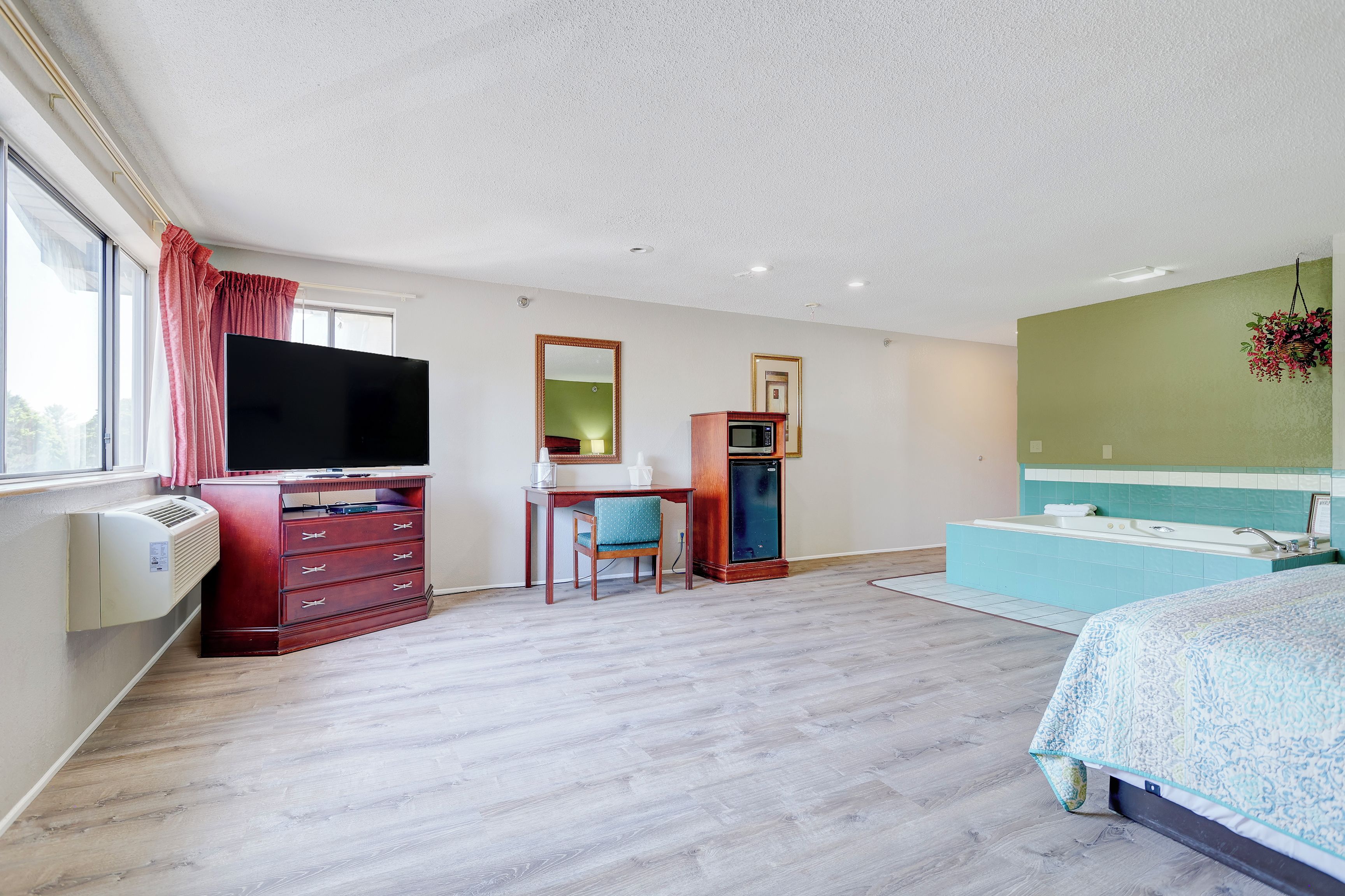 Quarto de hotel com uma cama grande, televisão, escrivaninha com cadeira, micro-ondas e banheiro pequeno com banheira.