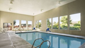 Piscina interior com vista desobstruída através de grandes janelas, área de estar à beira da piscina com cadeiras e um design arquitetônico simples e elegante.