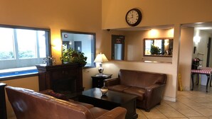 Uma sala de estar com lareira, sofás de couro, uma mesa de centro, um relógio e vista para o exterior.