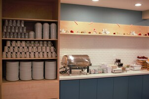 Buffet montado com pratos e tigelas empilhados, um espaço para café e uma parede decorativa com objetos pendurados.