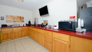 Uma cozinha com armários de madeira, micro-ondas, cafeteira e televisão presa na parede.