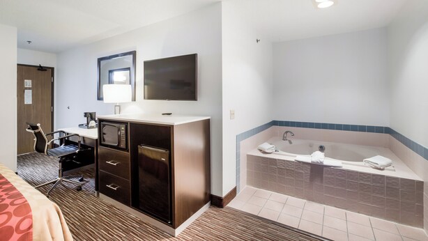 Quarto de hotel com cama, escrivaninha com cadeira, micro-ondas, frigorífico e uma banheira grande.