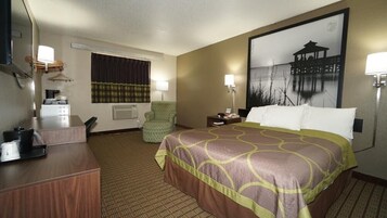 Quarto de hotel com uma cama grande, uma escrivaninha, uma cadeira, um abajur e um quadro na parede.
