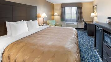 Quarto de hotel com uma cama grande, duas luminárias de cabeceira, uma escrivaninha, uma cadeira e uma janela com cortinas.