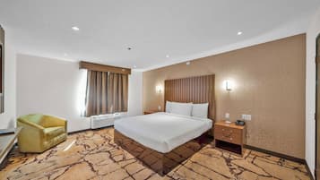 Quarto de hotel com uma cama grande, mesa de cabeceira, uma cadeira e janela com cortinas.