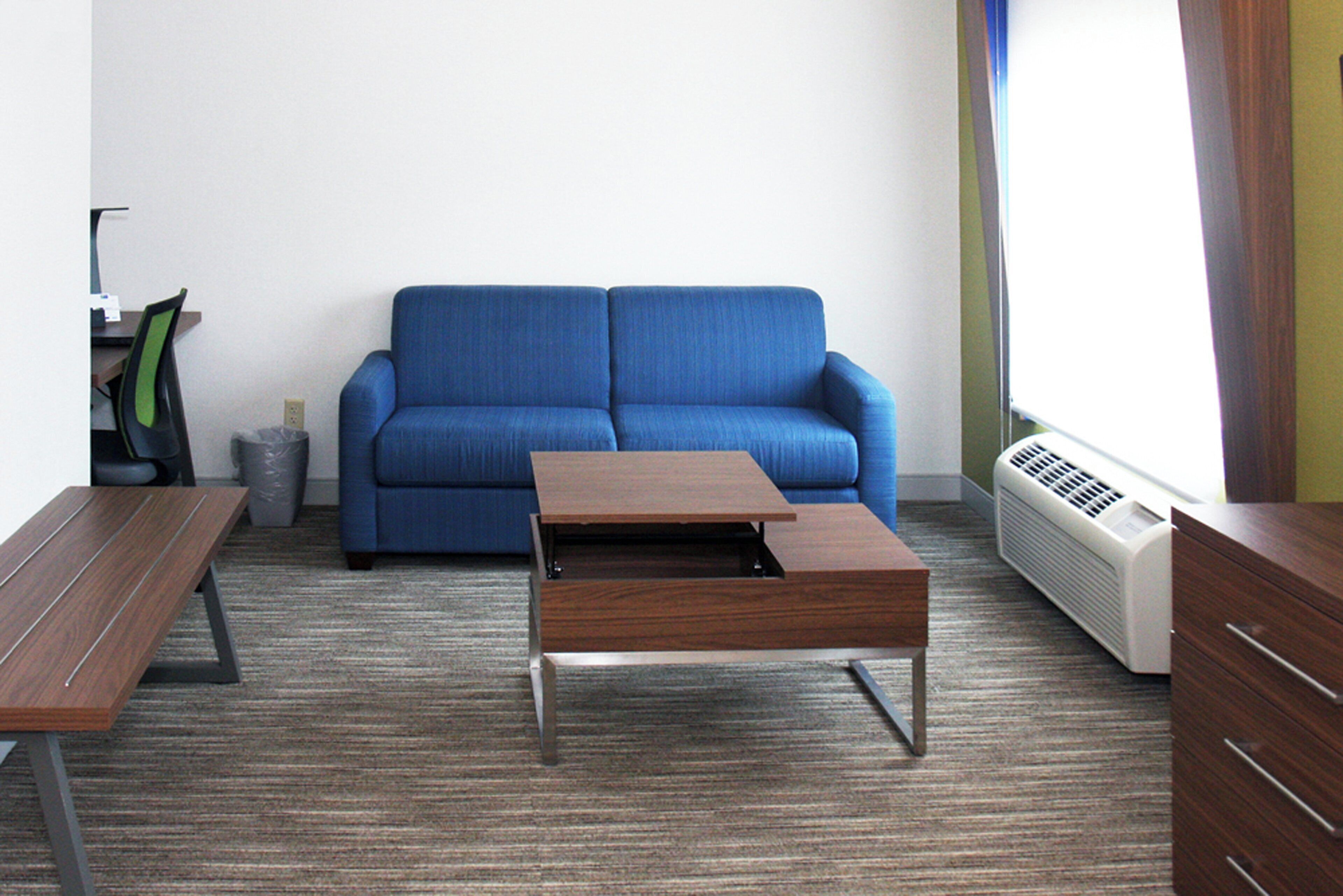 Quarto com sofá azul, mesa de centro de madeira, escrivaninha e radiador.