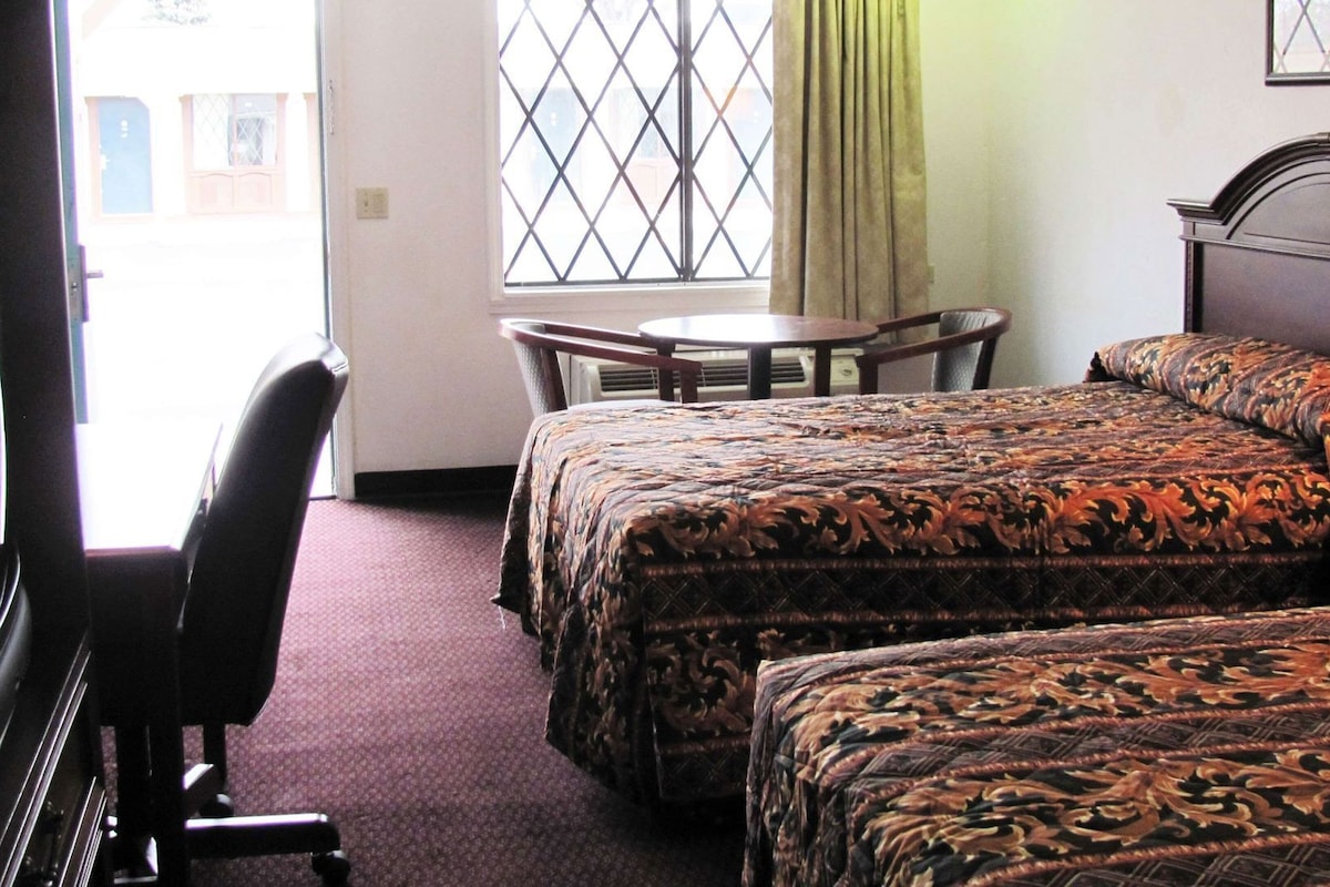 Quarto de hotel com duas camas, uma escrivaninha, uma cadeira e janela com vista.