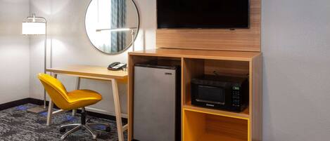 Quarto de hotel com escrivaninha, cadeira, televisão, frigorífico e micro-ondas.