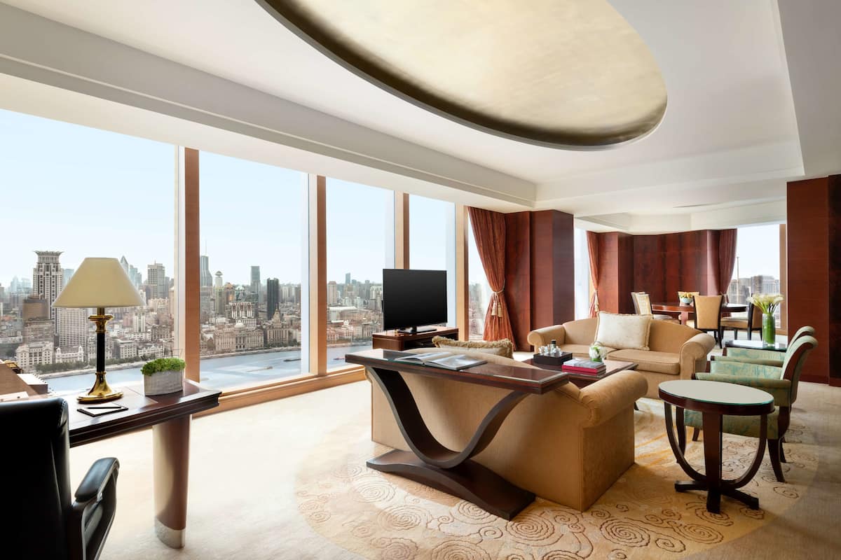 Quarto de hotel espaçoso com vista ampla para a cidade, um sofá confortável, uma escrivaninha com abajur e uma televisão.
