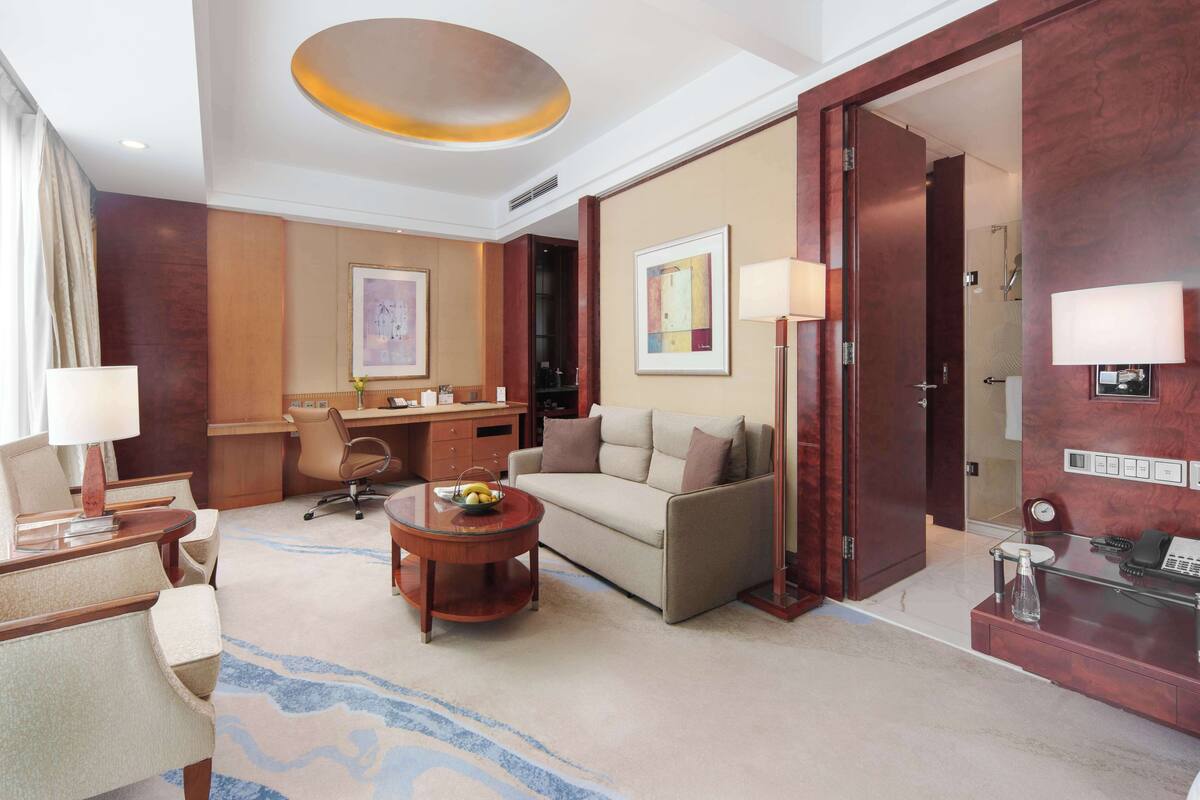 Quarto de hotel com sofá, escrivaninha, mesa de centro e uma cadeira.