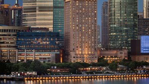 Horizonte urbano com arranha-céus modernos, incluindo um edifício com a placa 'Shanghai', refletindo na água.