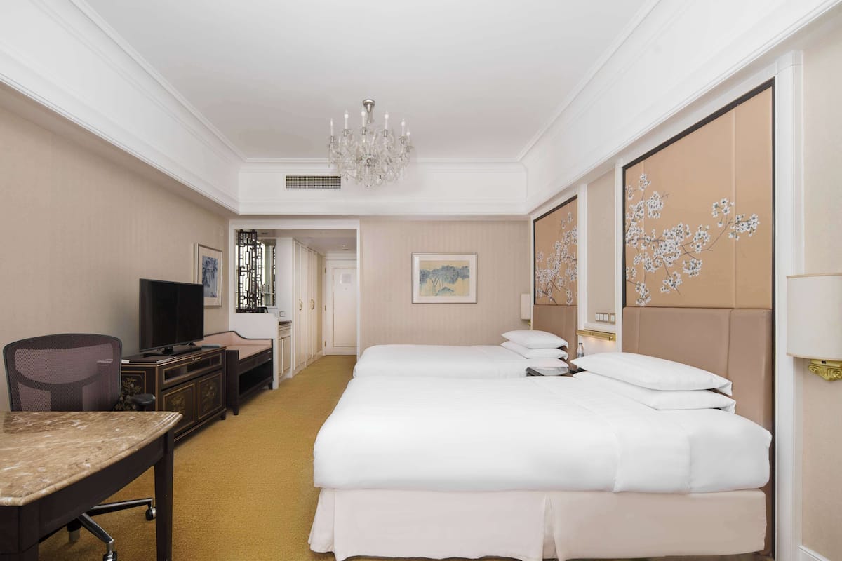 Quarto de hotel com uma cama grande, uma escrivaninha com cadeira, uma televisão e um painel decorativo na parede.