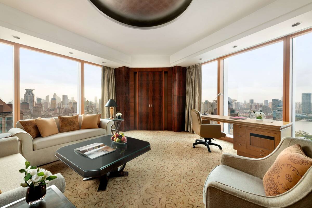 Quarto de hotel moderno com vista ampla da cidade, um sofá, uma escrivaninha e uma mesa de centro.