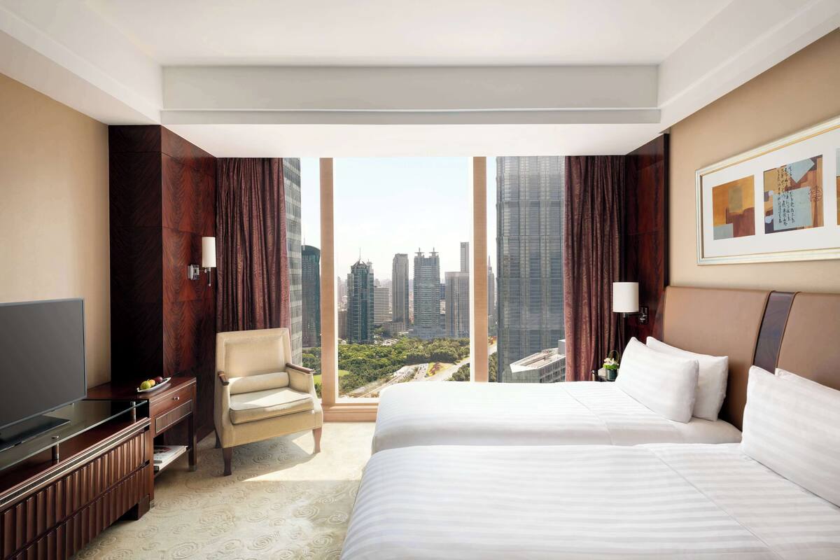 Quarto de hotel com uma cama grande, televisão, uma cadeira e vista para a cidade.