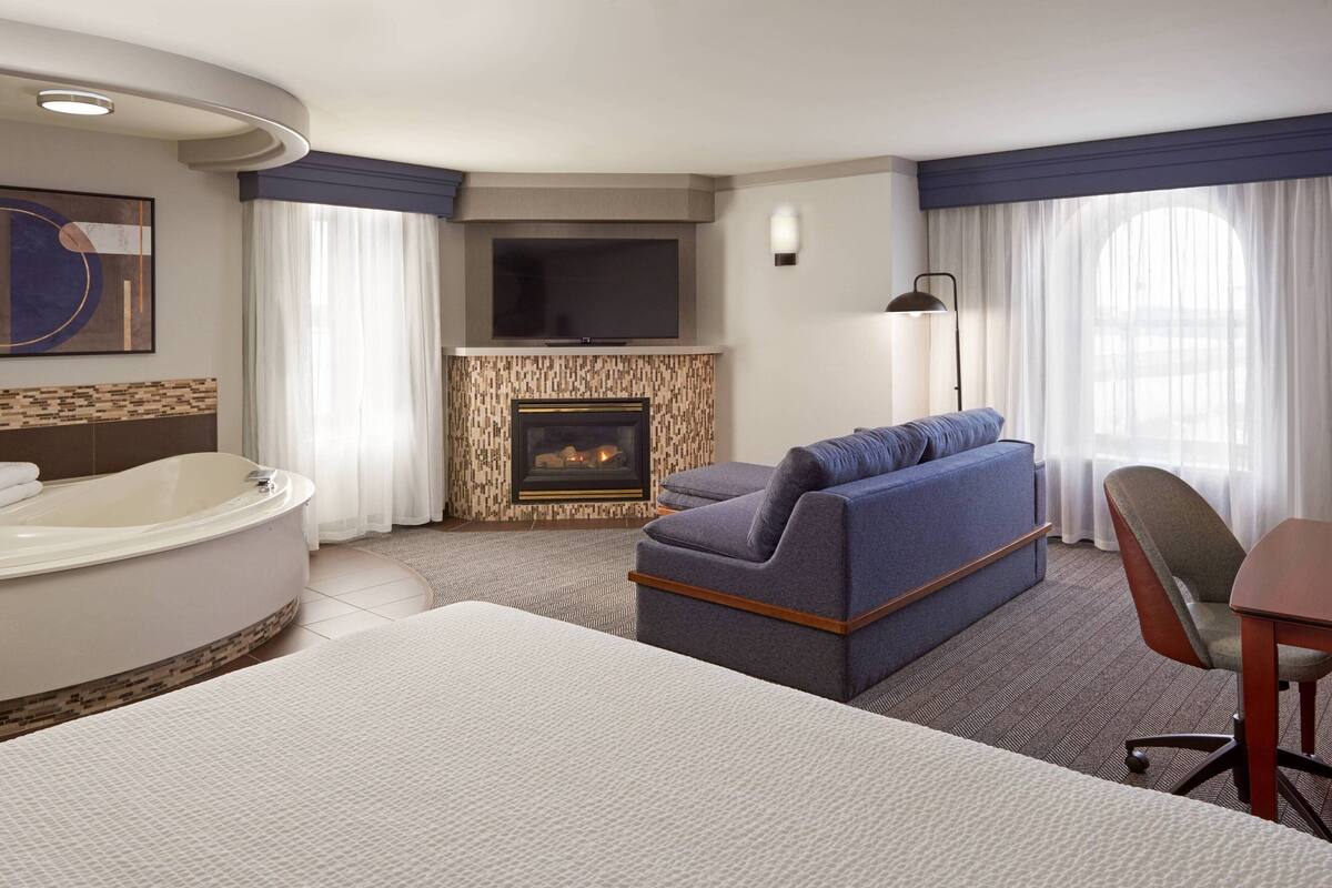 Quarto de hotel com uma cama grande, um sofá, uma poltrona, uma lareira e uma televisão.