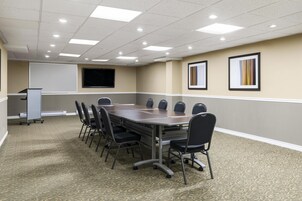 Uma sala de conferências com uma mesa comprida, cadeiras, tela de projetor e quadros nas paredes.