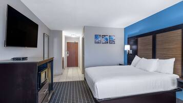Quarto de hotel com cama, televisão, escrivaninha e porta para um corredor.