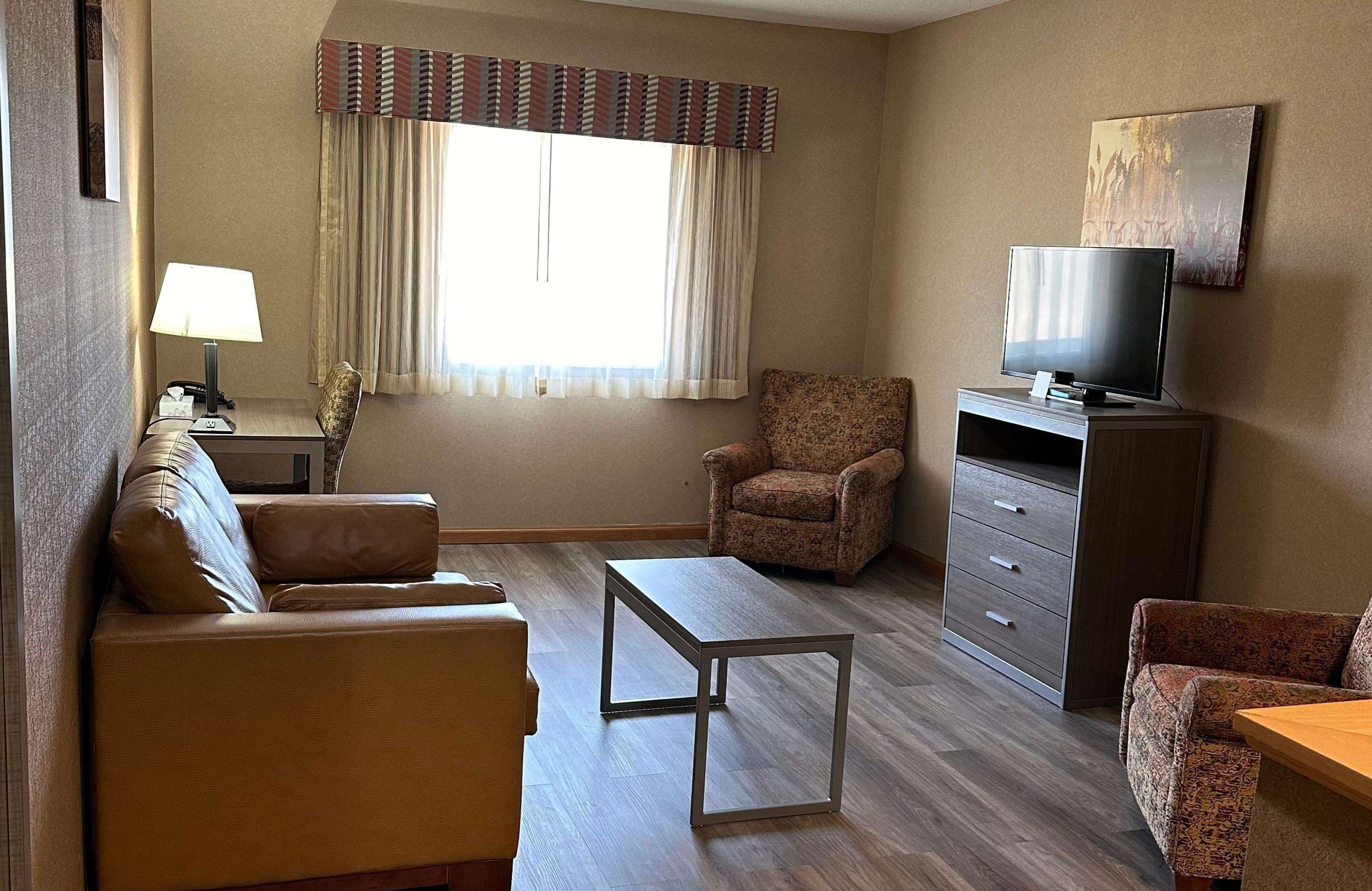 Quarto de hotel com sofá, poltrona, mesa de centro, televisão e cômoda.