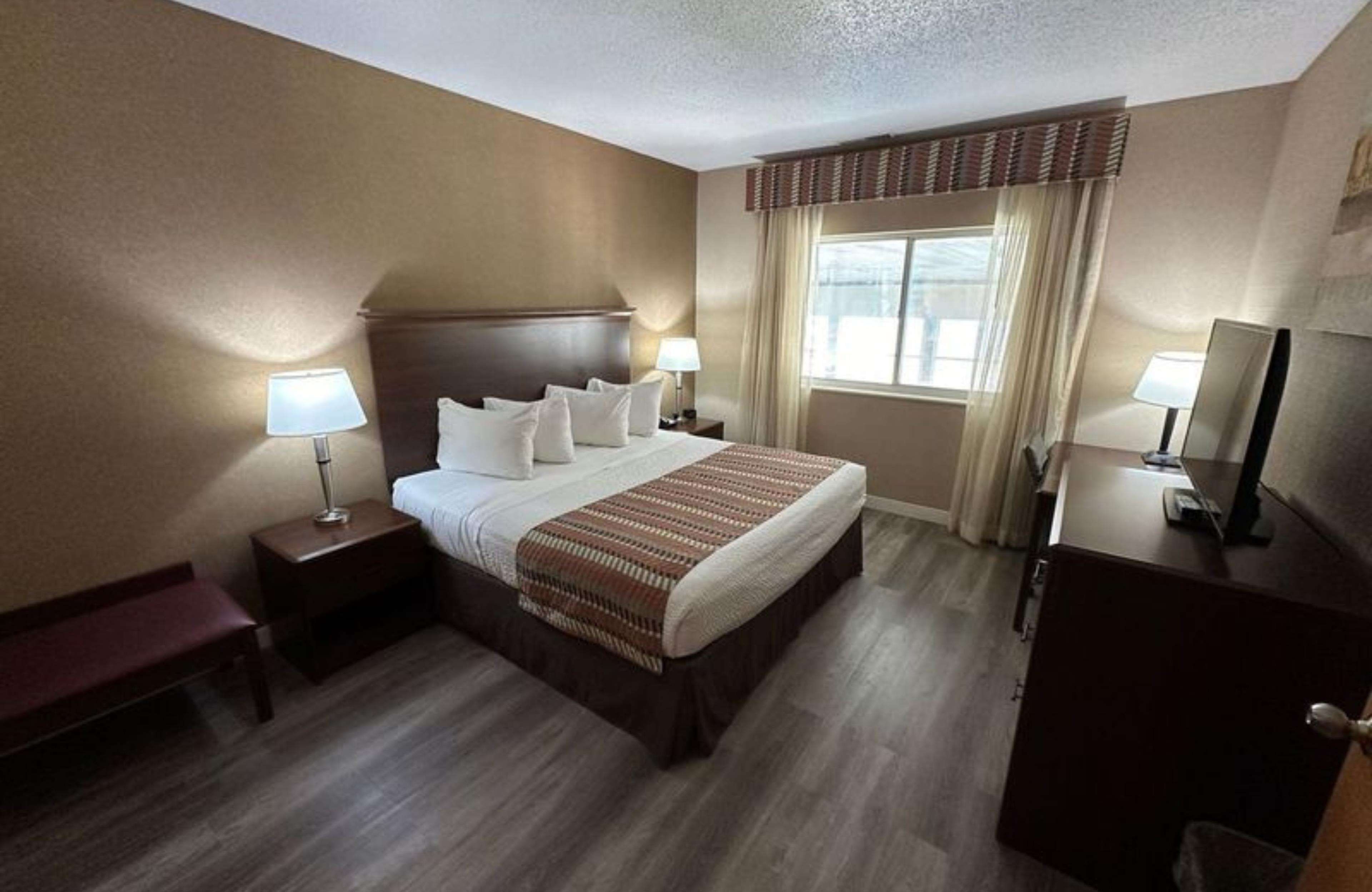 Quarto de hotel com uma cama grande, duas mesas de cabeceira com abajures, cômoda e janela com cortinas.