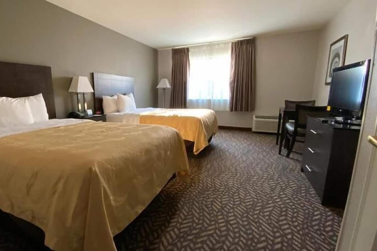 Quarto de hotel com duas camas, uma escrivaninha, televisão e uma janela com cortinas.