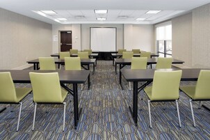 Sala de conferências com mesas, cadeiras, tela de projeção e carpete estampado.