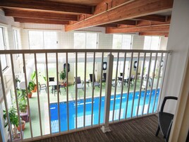 Uma varanda com vista para uma piscina, vigas de madeira e plantas em vasos.