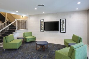 Um hall com escada, assentos estofados verdes, TV de tela plana e carpete estampado.
