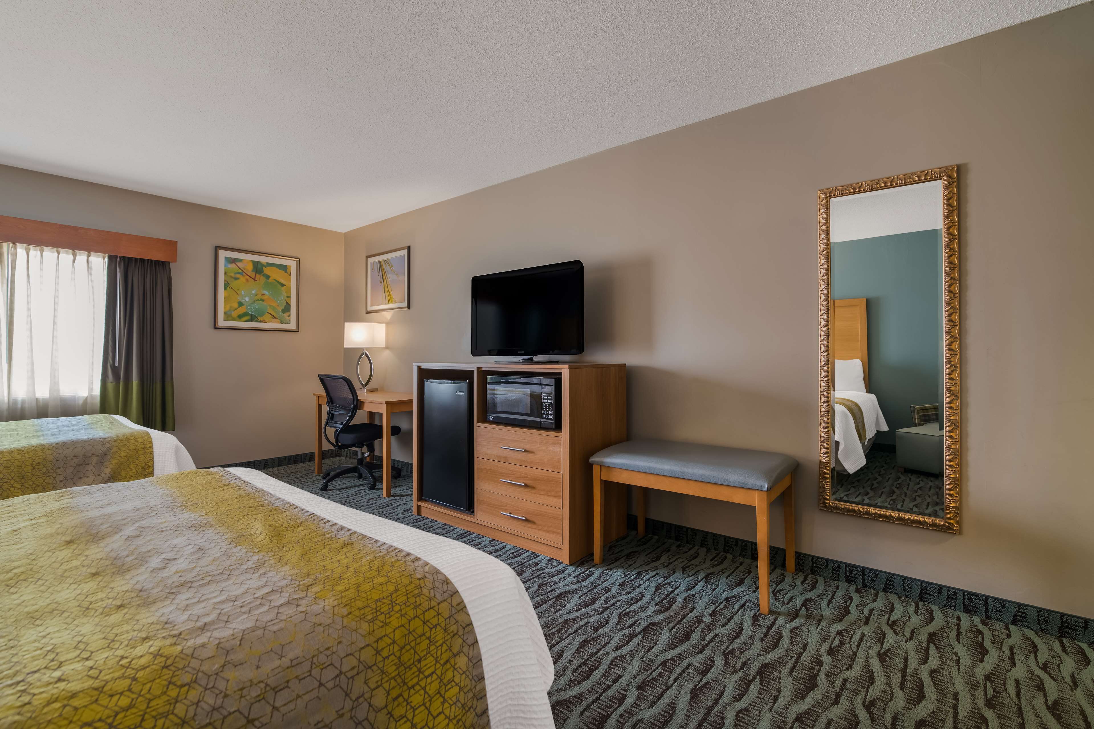 Quarto de hotel com duas camas, uma escrivaninha com computador, televisão, espelho e um pequeno armário.