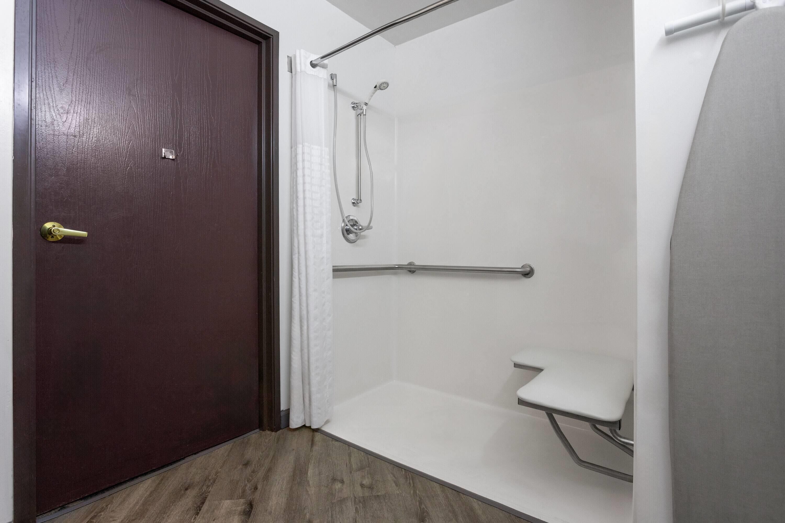 Uma área de chuveiro com porta de vidro, um banco branco e barra de apoio.
