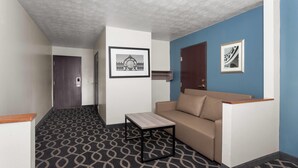 Quarto de hotel com carpete estampado, um sofá, uma mesa pequena e duas molduras na parede.