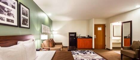 Quarto de hotel com cama, escrivaninha, cadeira, cozinha compacta e banheiro.