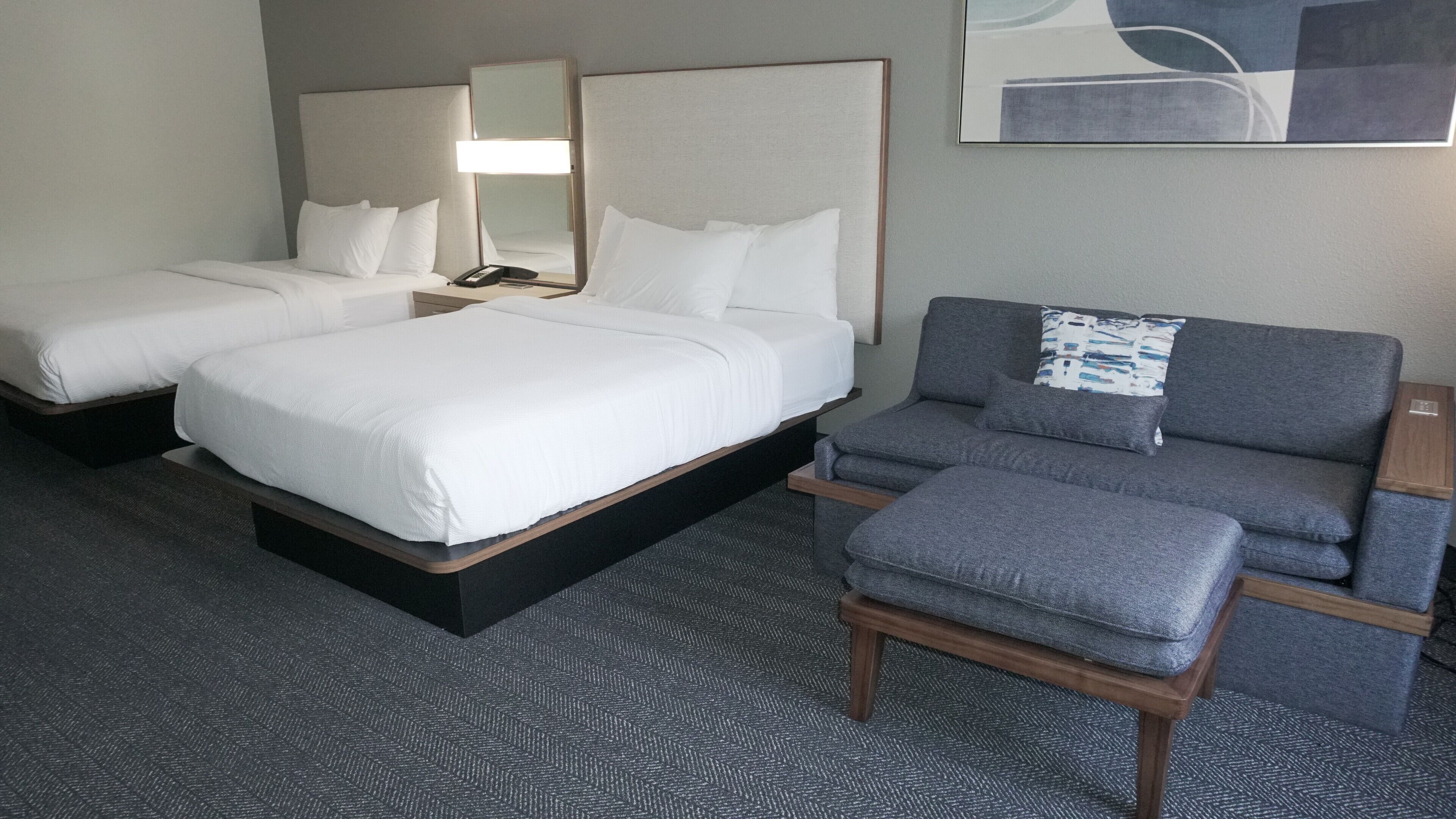 Quarto de hotel com uma cama grande, duas mesas de cabeceira, uma cadeira e um espelho.