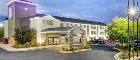 Um hotel Sleep Inn com design moderno, destacando uma entrada imponente, área de estacionamento coberta e um gramado bem cuidado.