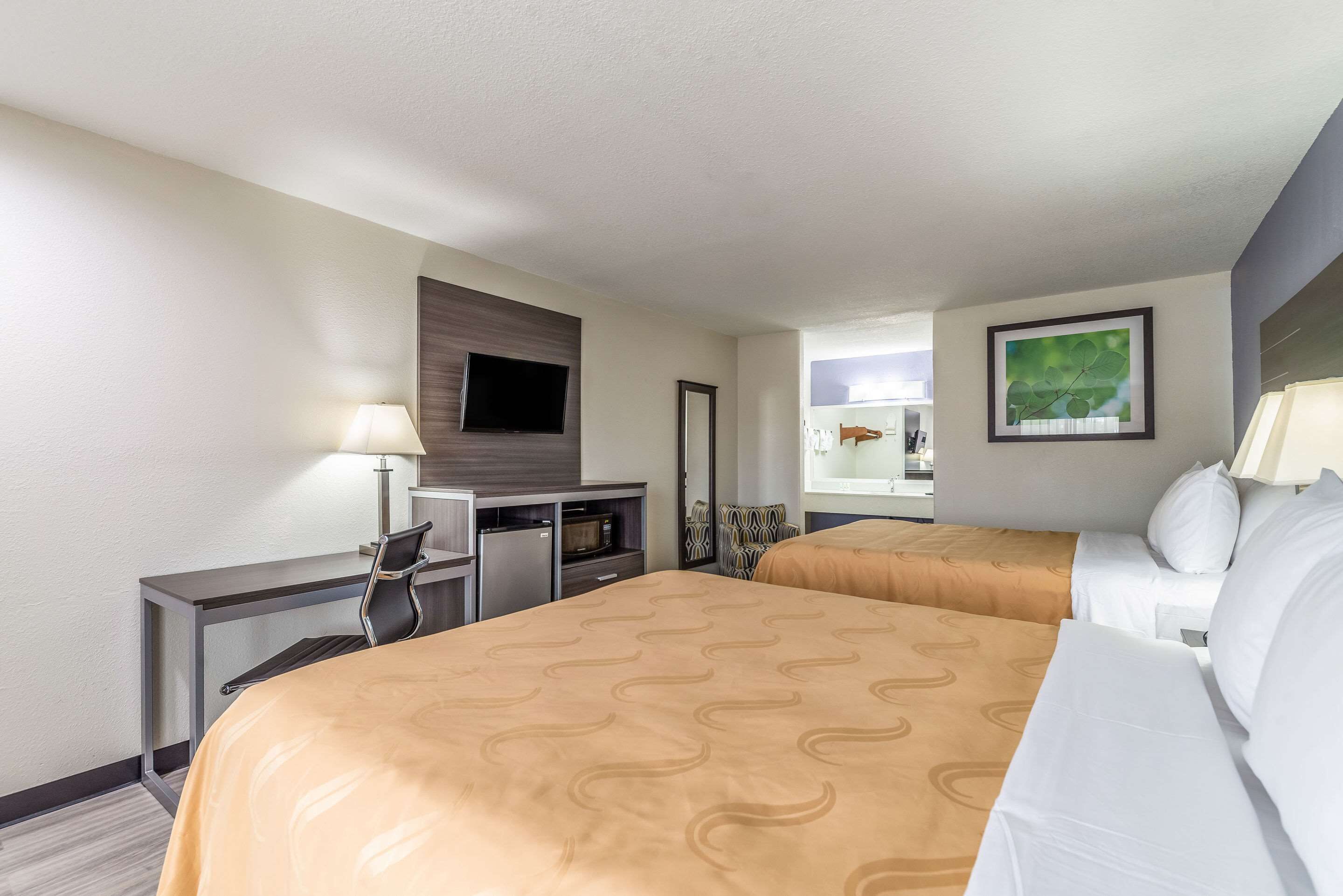 Quarto de hotel com duas camas, uma mesa com televisão de tela plana, um espelho e uma janela com vista.
