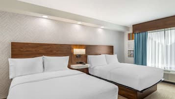 Quarto de hotel com duas camas, cabeceira de madeira, mesa de cabeceira com abajur e janela com cortinas.