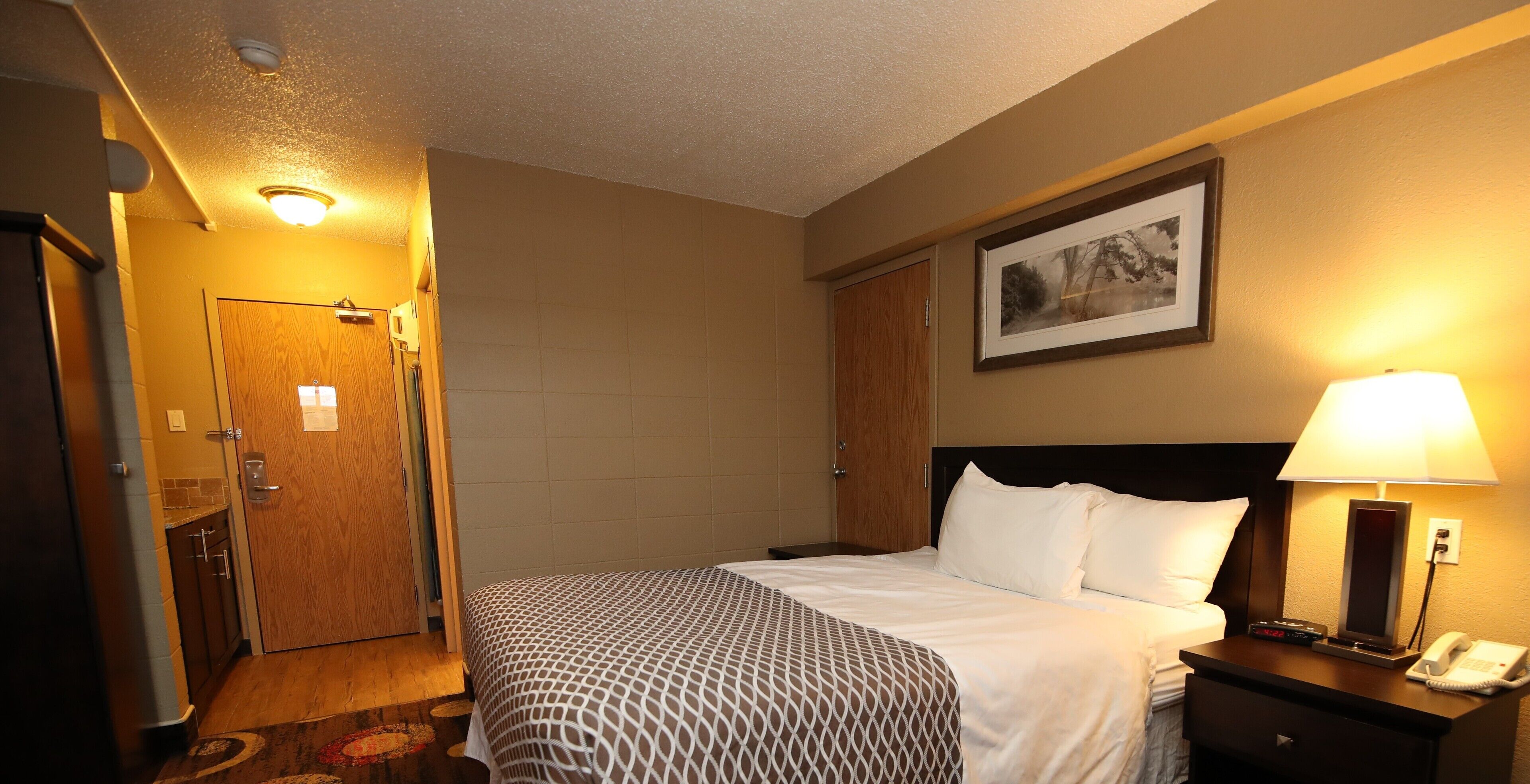 Quarto de hotel com cama, mesa de cabeceira, luminária e um quadro na parede.