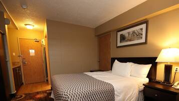 Quarto de hotel com cama, mesa de cabeceira, luminária e um quadro na parede.